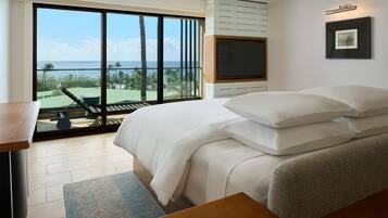 Quarto com uma grande janela, cama com roupa de cama branca, TV e vista para o oceano.
