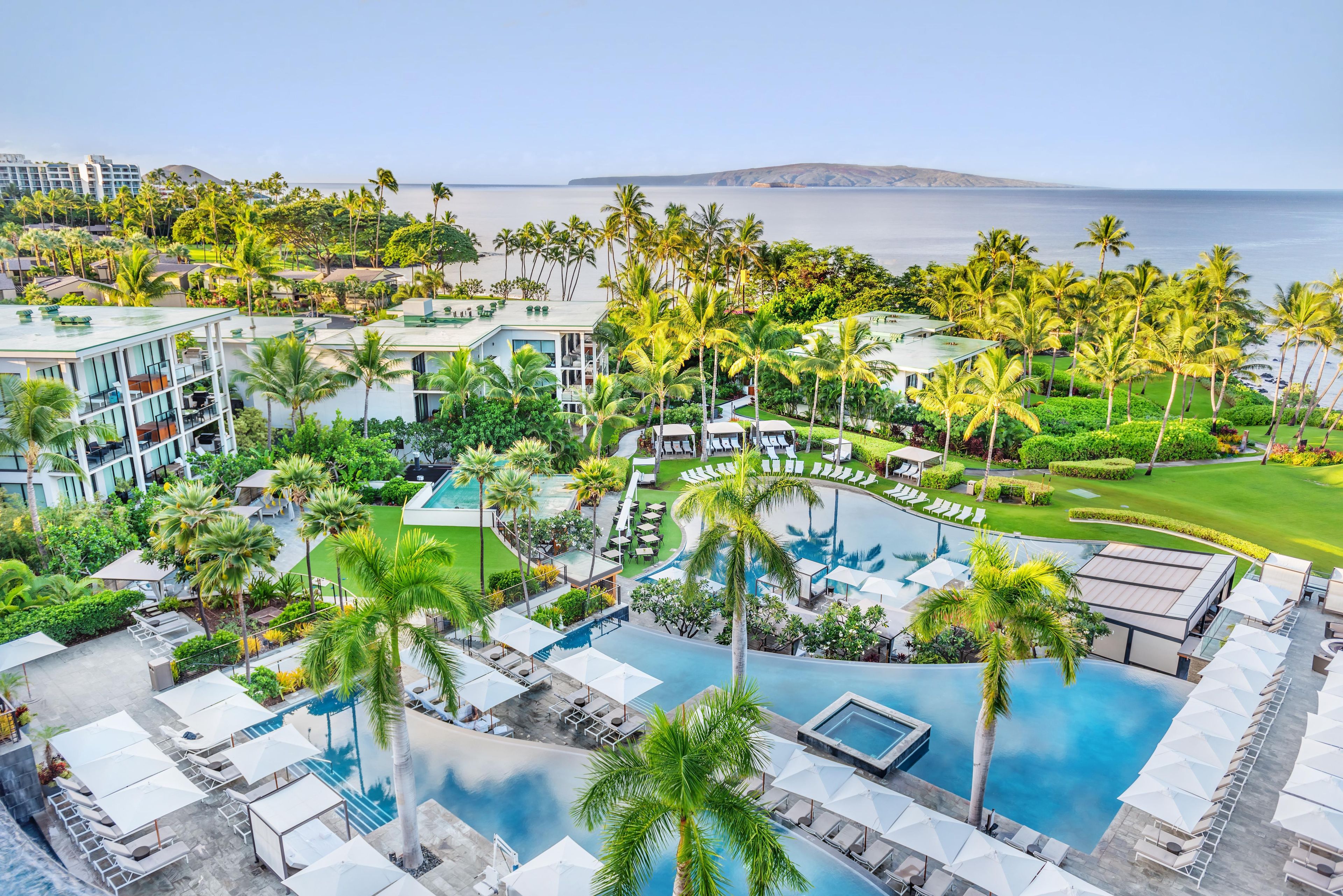 Resort com várias piscinas, palmeiras e vista para o oceano.