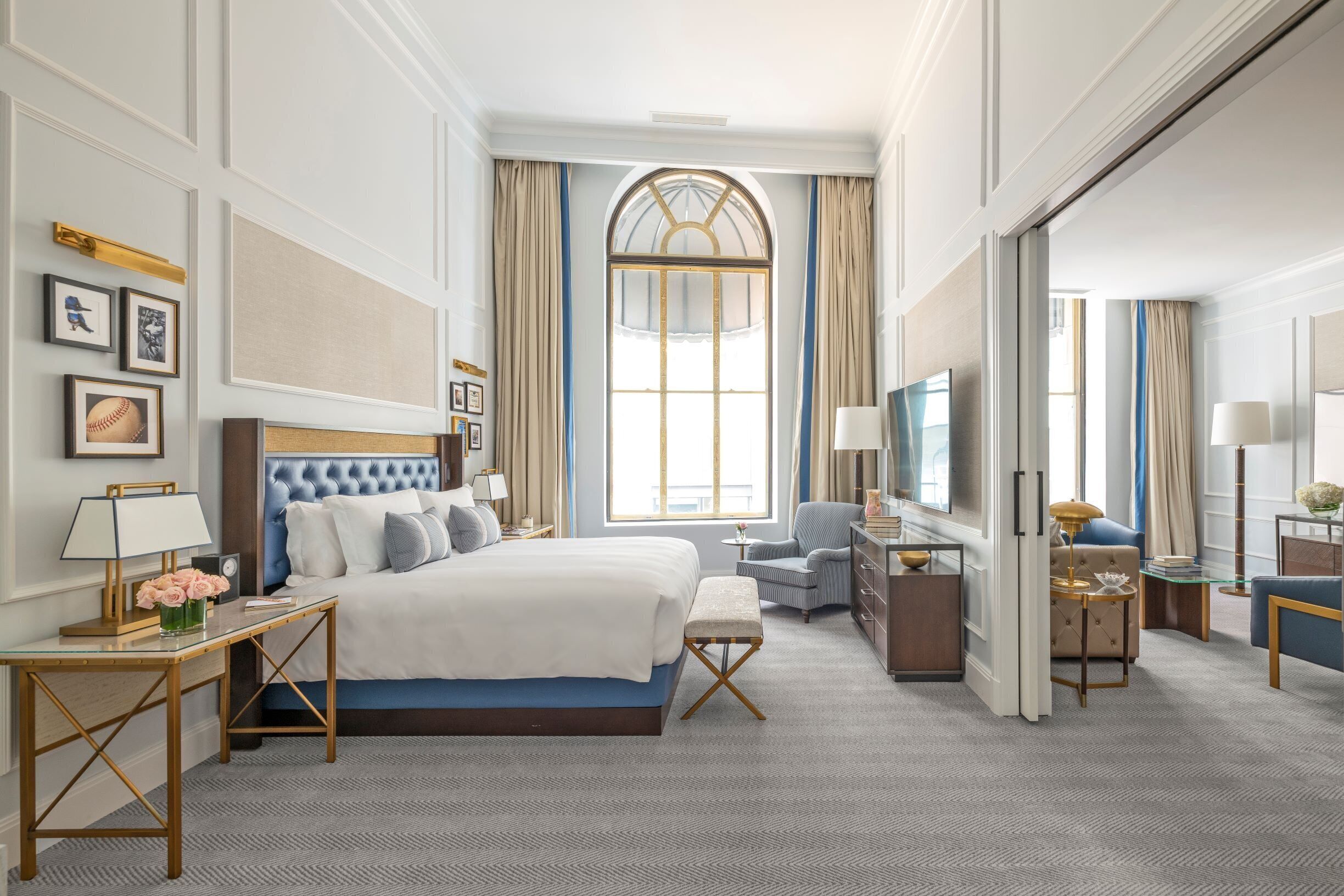 Quarto de hotel com uma cama grande, uma mesa, uma cadeira, uma televisão e uma janela com cortinas.
