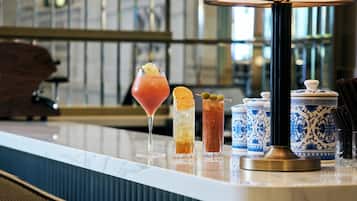Uma área de bar com bancada de mármore, uma luminária branca e três bebidas.