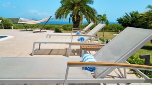 Área de piscina com espreguiçadeiras e uma rede.