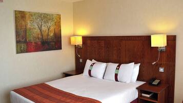 Quarto de hotel com cama, duas luminárias de cabeceira, um quadro na parede e mesa de cabeceira com telefone.