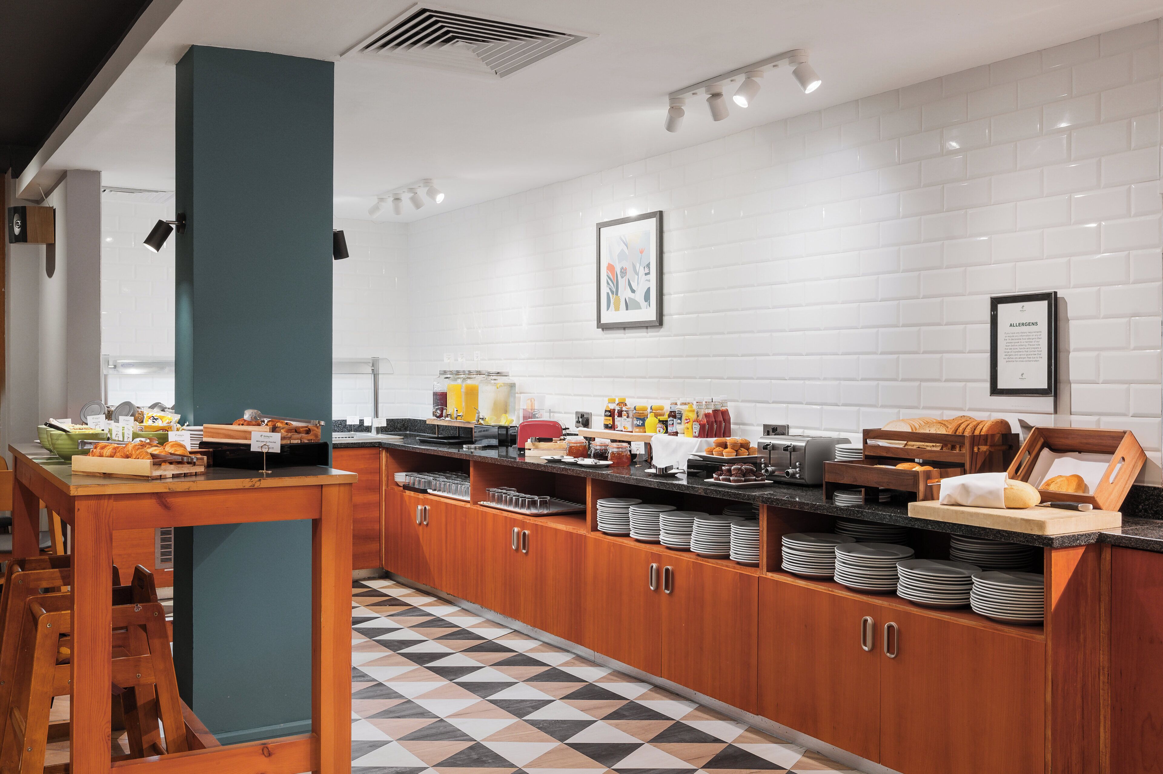 Uma cozinha moderna com piso xadrez, armários de madeira e diversos itens de café da manhã sobre o balcão.