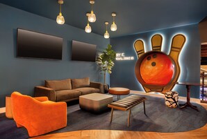 Uma sala de estar moderna com um mural de pinos de boliche, um sofá marrom, poltronas laranjas e uma mesa de centro de madeira.