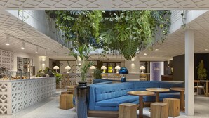 Espaço de lounge moderno com um sofá azul, banquinhos de madeira e plantas pendentes.