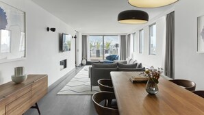 Quarto de hotel moderno com uma mesa de jantar de madeira, um sofá e uma grande janela com vista para o exterior.