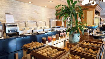 Uma área de buffet com diversos alimentos, uma máquina de café e uma grande planta em vaso.