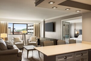Quarto de hotel moderno com sofá, mesa de jantar, televisão de tela plana e vista para a cidade.