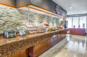 Um buffet de café da manhã com diversos alimentos, uma parede de pedra e uma placa com a inscrição 'Breakfast Corner'.