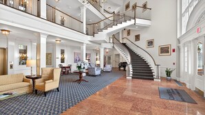 Um hall amplo com uma escadaria imponente, várias áreas de estar e um balcão de recepção.