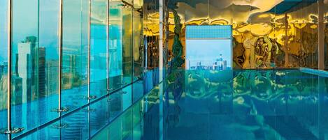 Um interior moderno com paredes de vidro refletivas, vista para a cidade e arte abstrata nas paredes.