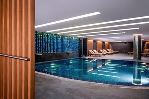 Uma área de piscina interna moderna, com piscina transparente, espreguiçadeiras e uma parede decorativa.