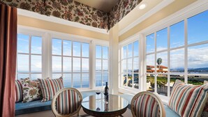Quarto com uma grande janela panorâmica com vista deslumbrante, uma mesa redonda com cadeiras e um sofá com almofadas listradas.