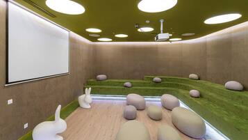Uma sala de conferências moderna com carpete verde, esculturas de coelhos brancos e uma tela de projetor.