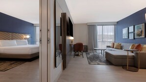 Quarto de hotel moderno com uma cama, um sofá, um espaço para refeições e uma janela grande.