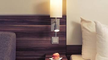 Quarto de hotel com cabeceira de madeira, mesa de cabeceira com abajur, travesseiro e uma fruta sobre a mesa.
