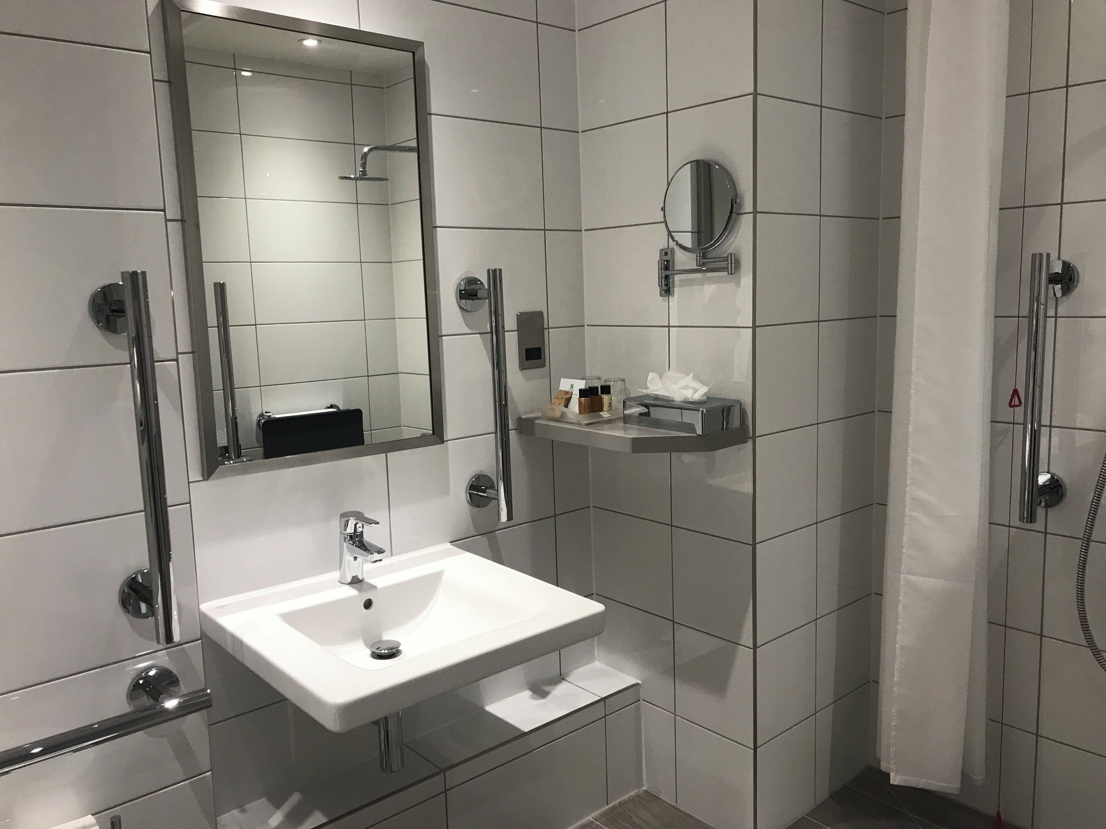 Uma casa de banho moderna com uma pia branca, um espelho, chuveiro e um porta-toalhas.