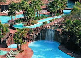 Um resort com várias piscinas, uma cascata e palmeiras.