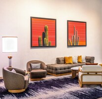 Uma sala de estar com sofá, poltronas, luminária e duas obras de arte emolduradas.