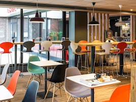 Interior moderno de café com várias mesas e cadeiras, área de bar e grandes janelas com vista para a rua.