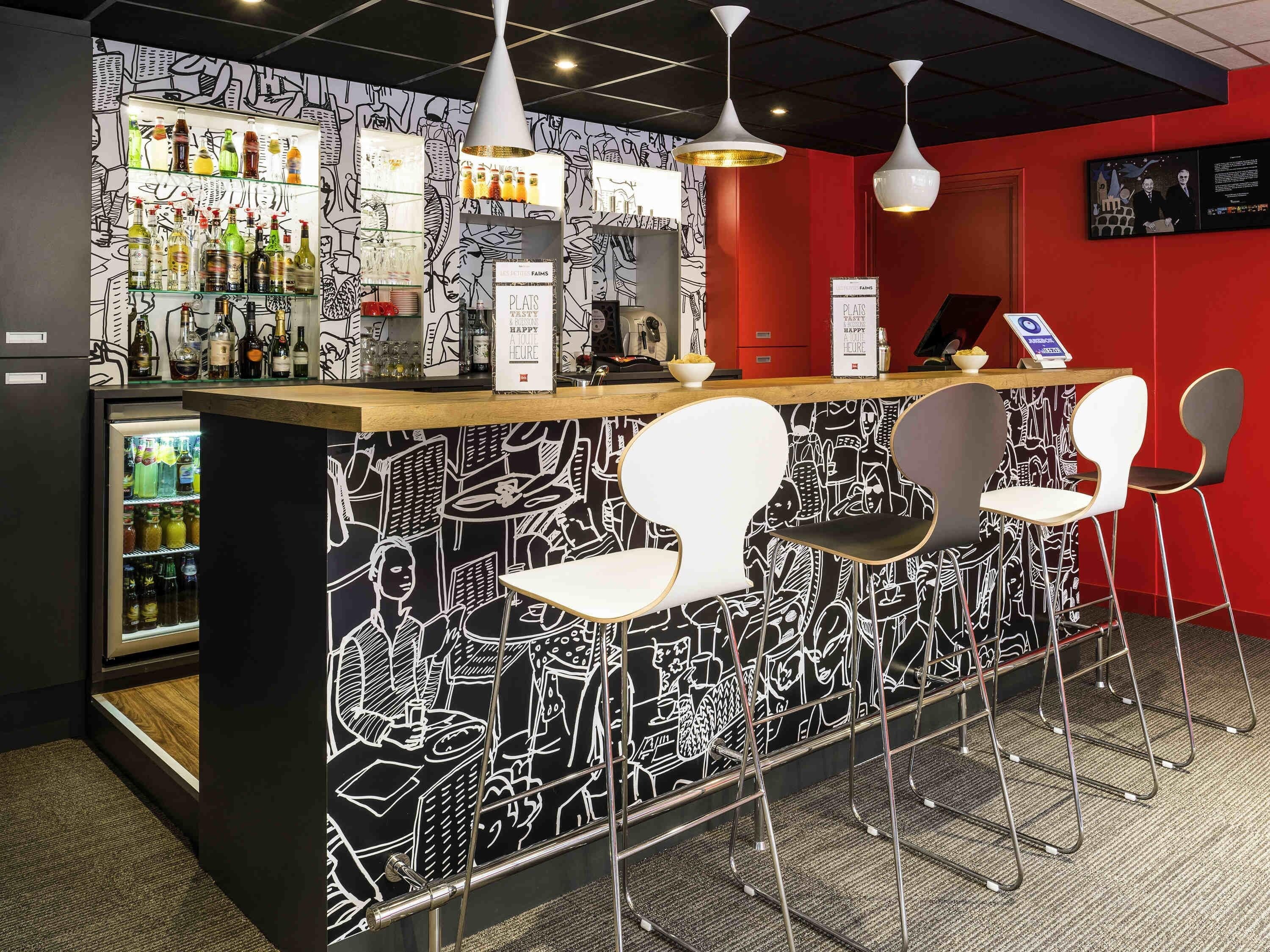 Uma área de bar com um mural em preto e branco, um refrigerador com bebidas e banquetas de bar modernas.