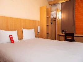 Quarto de hotel com cama, guarda-roupa e uma pequena mesa.