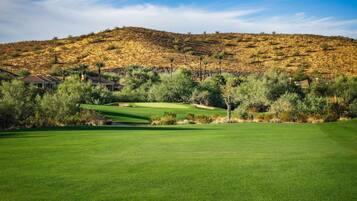 Um campo de golfe sob um céu claro, com um green bem cuidado e um cenário montanhoso ao fundo.