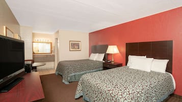 Quarto de hotel com duas camas, televisão, secretária e casa de banho com espelho e iluminação.