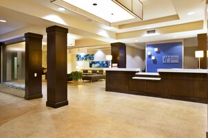 Um saguão de hotel com balcão de recepção, área de estar e uma janela ampla.
