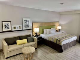 Quarto de hotel com cama, sofá, mesa redonda pequena e luminárias fixadas na parede.
