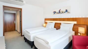 Quarto de hotel com duas camas, uma cadeira vermelha, uma cabeceira de madeira e uma obra de arte pendurada na parede.