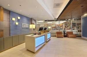 Uma área de recepção de hotel com design moderno, incluindo um balcão de atendimento, zona de estar e obras de arte nas paredes.