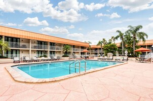 Um hotel com piscina, área externa para descanso e palmeiras.