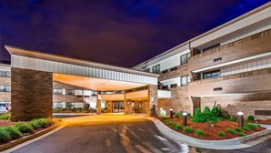 Hotel com vários andares, entrada central, área de estar ao ar livre e jardim ajardinado.
