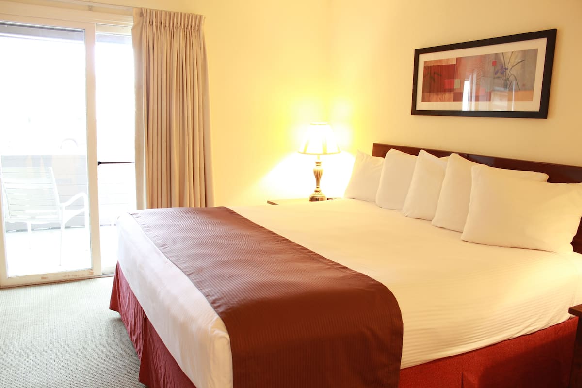 Quarto de hotel com uma cama grande, uma luminária de cabeceira, um quadro na parede e uma porta de vidro deslizante para uma área externa.
