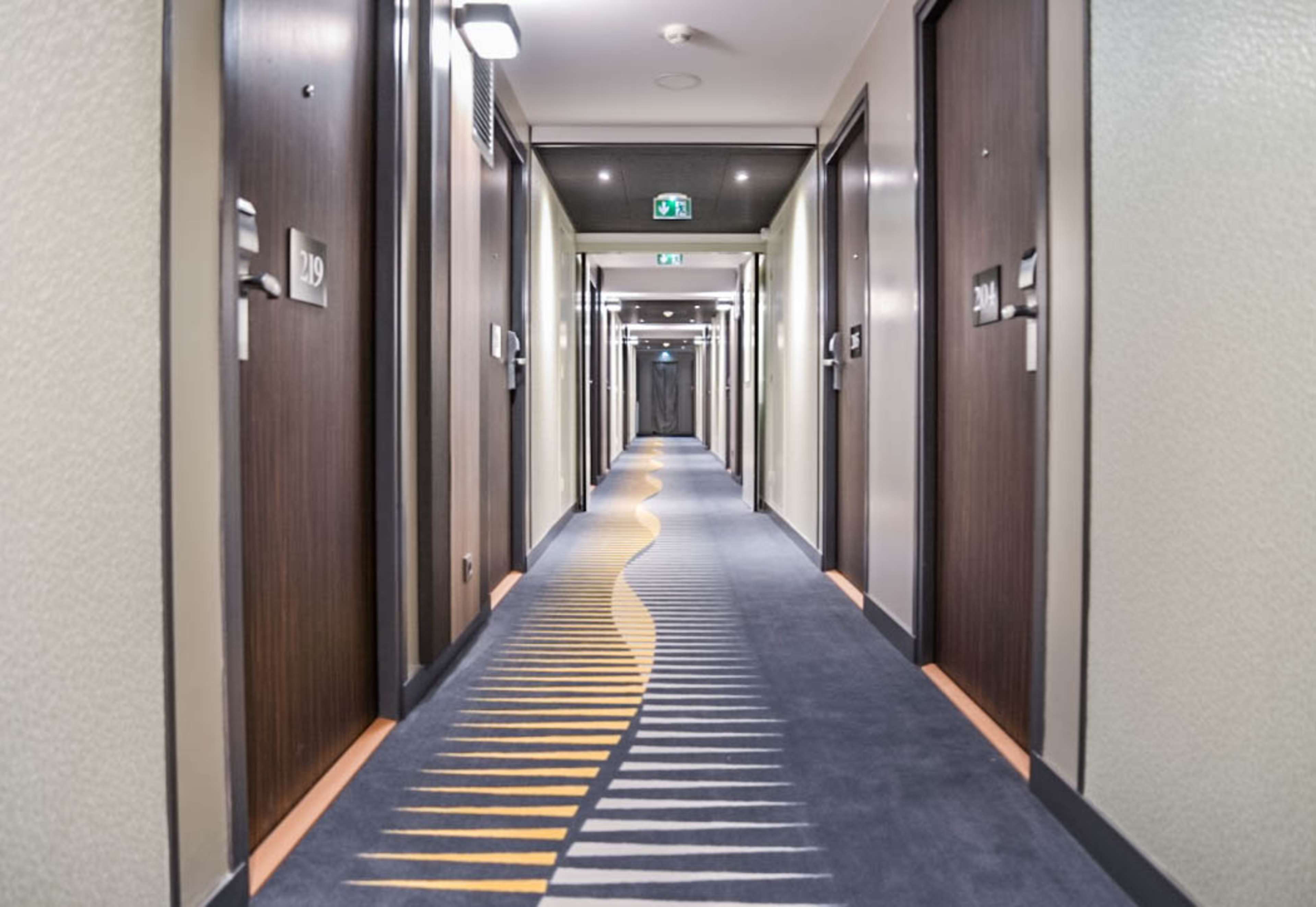 Corredor de hotel com portas numeradas 219 e 2204, carpete estampado e placa de saída de emergência.