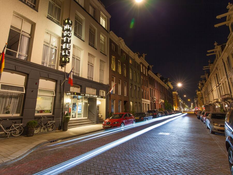 Um hotel com uma placa indicando "HOTEL CITY GARDEN" e um carro vermelho estacionado na rua.