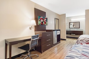 Quarto de hotel com escrivaninha, cadeira, cama, TV e espelho.