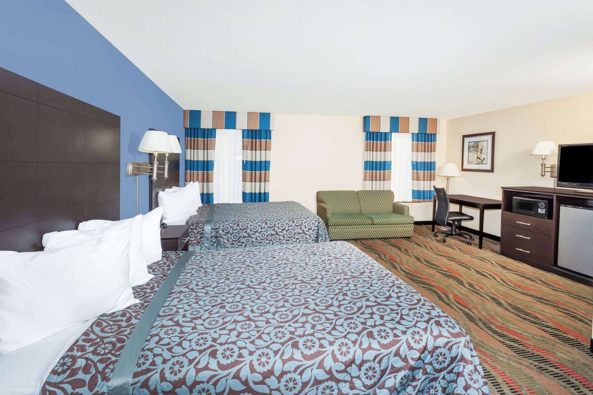 Quarto de hotel com duas camas, uma escrivaninha, uma cadeira e uma televisão.