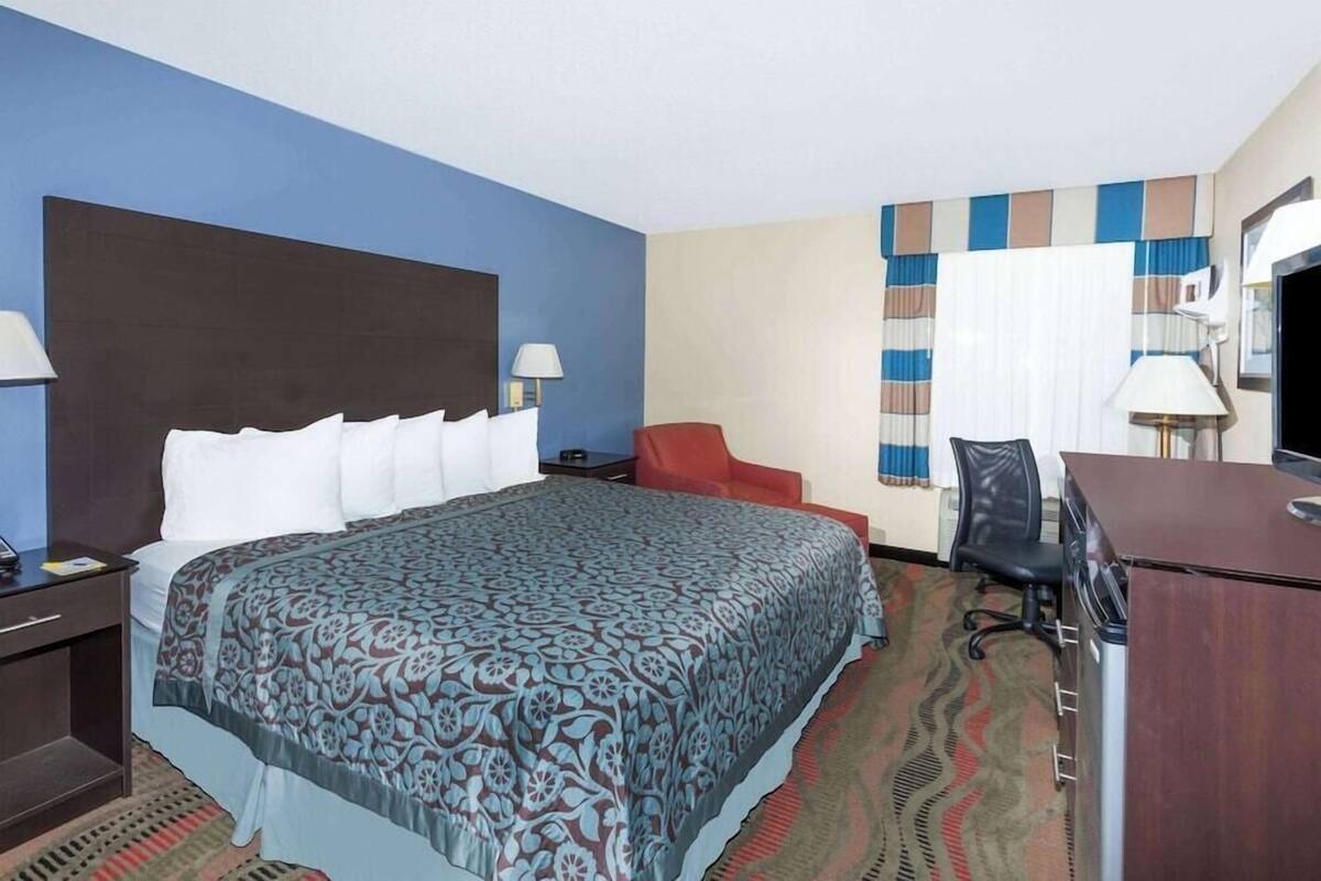 Quarto de hotel com uma cama grande, uma escrivaninha, uma cadeira e uma televisão.