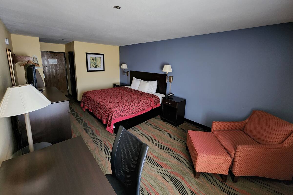 Quarto de hotel com cama, escrivaninha, cadeira, mesa de cabeceira e abajur.