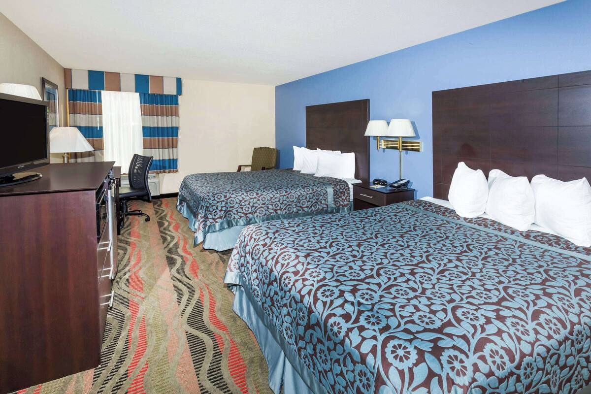 Quarto de hotel com duas camas, uma escrivaninha, uma cadeira, uma televisão e um abajur.