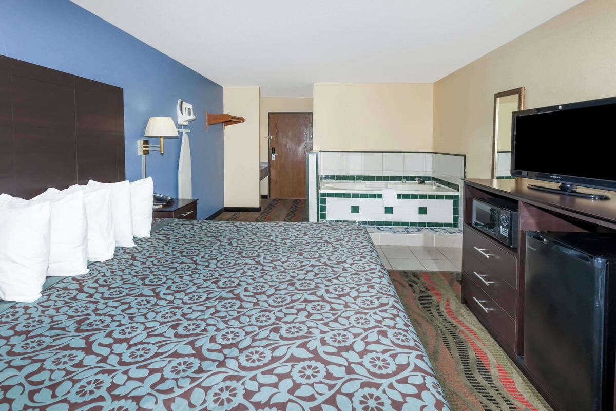 Quarto de hotel com cama, televisão, escrivaninha e casa de banho visível através de uma porta aberta.