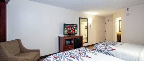 Quarto de hotel com duas camas, televisão, um pequeno armário e uma cadeira.