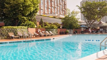 Piscina com espreguiçadeiras e vista para um edifício alto ao fundo.