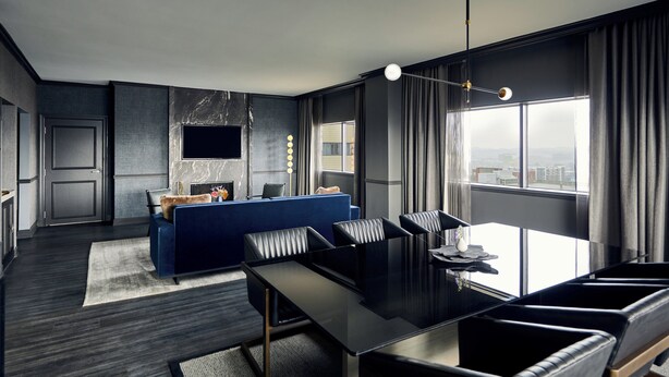 Quarto de hotel moderno com área de refeições, um sofá e uma TV fixada na parede.