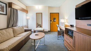 Quarto de hotel com sofá, mesa pequena, televisão, micro-ondas e armário de madeira.