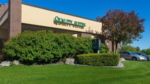 Um hotel chamado "Quality Suites", com uma placa, um gramado bem cuidado e um estacionamento cheio de carros.