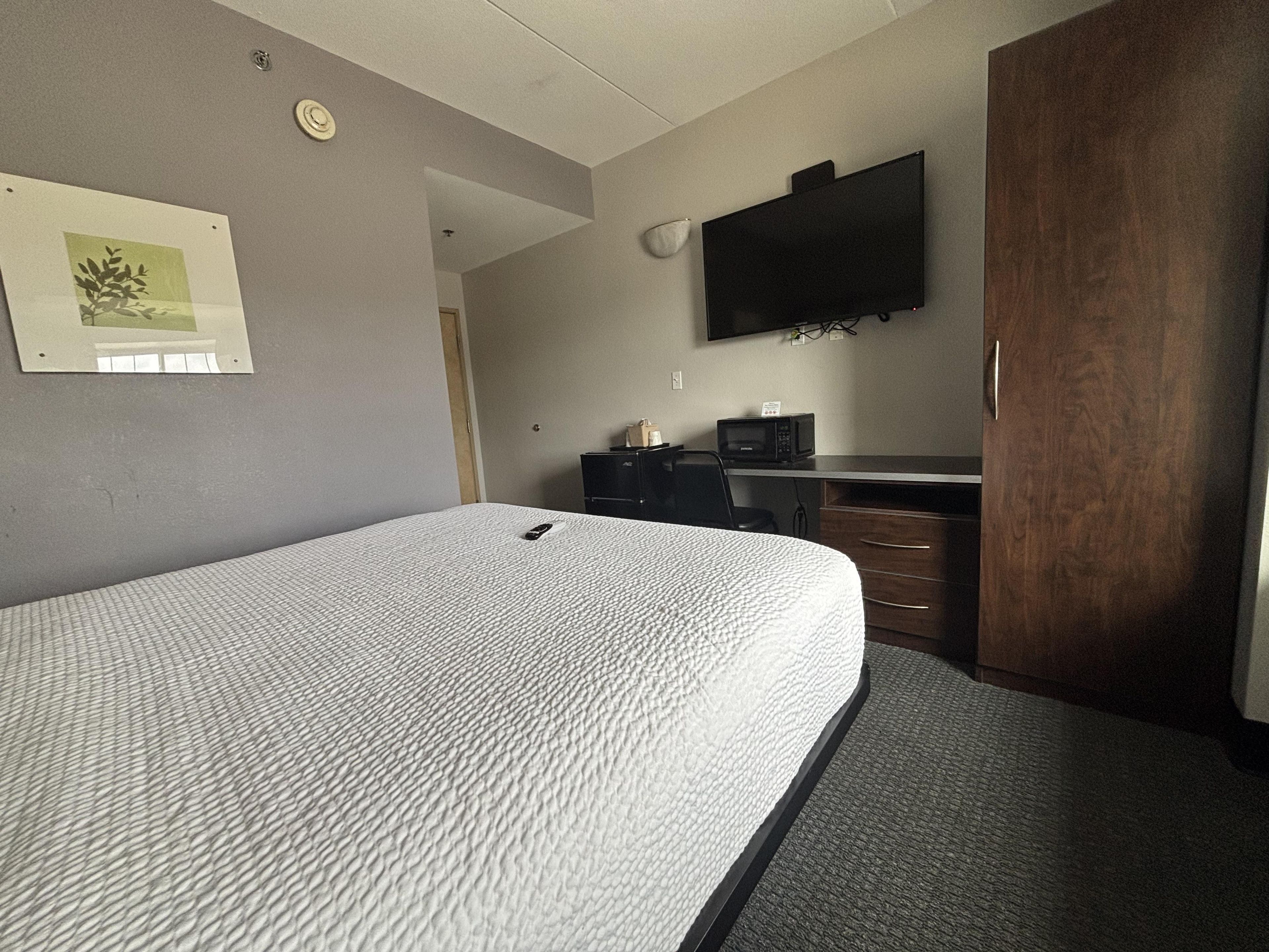 Quarto de hotel com cama, escrivaninha, televisão e micro-ondas.