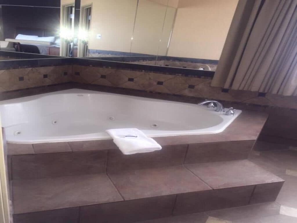 Casa de banho com uma banheira grande, espelho e chão em mosaico.